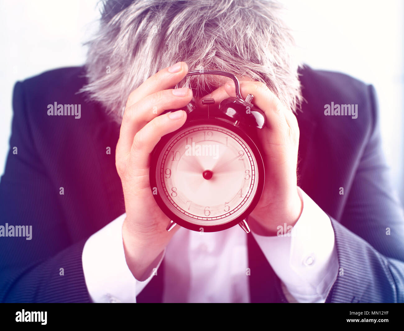 Man hiding face behind alarm clock on white background. Time management ...