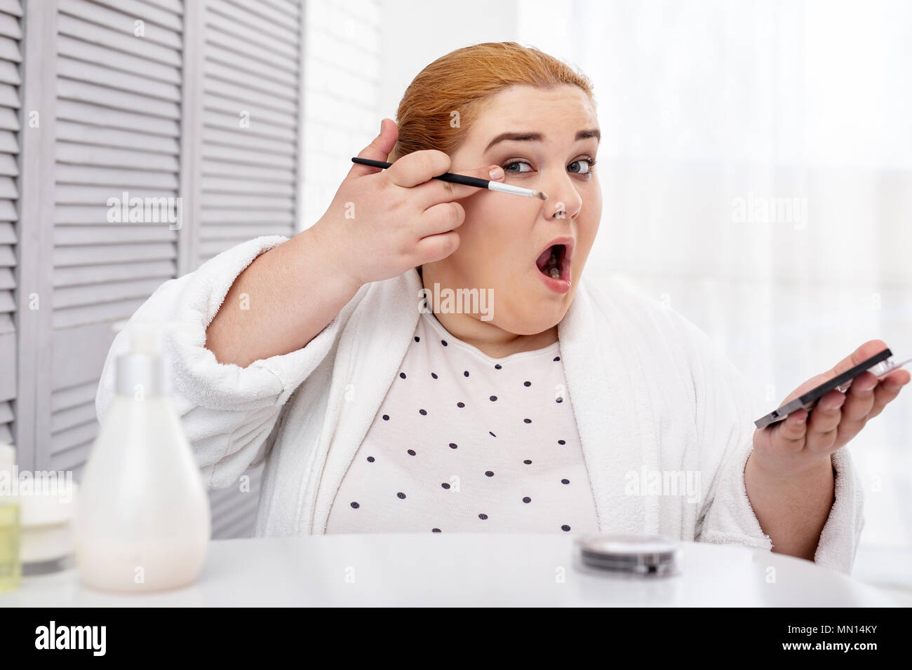 Concentrated stout woman applying make-up Stock Photo - Alamy