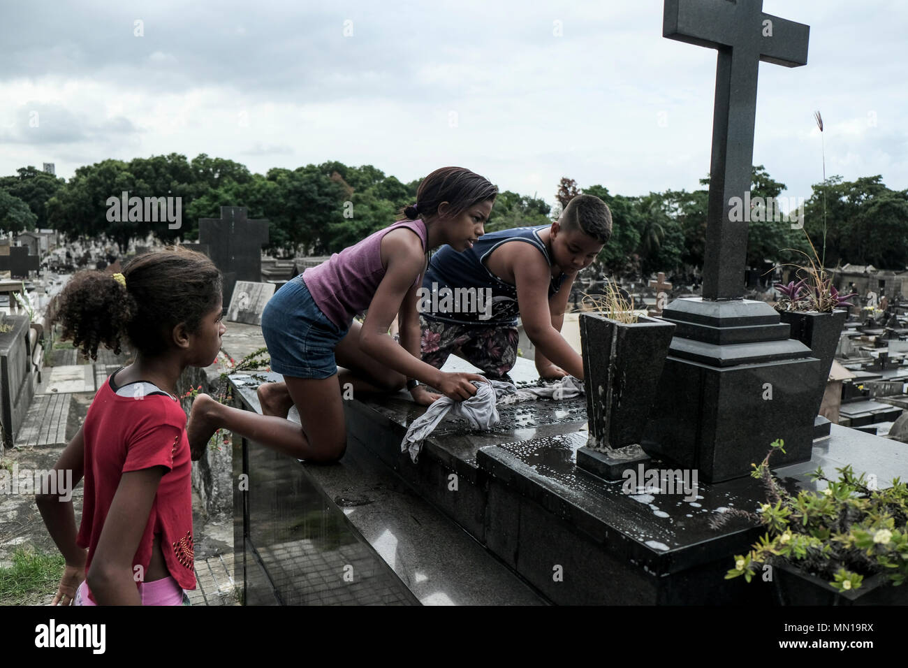 13 May 2018, Brazil, Rio de Janeiro: A boy and two girls clean a grave ...