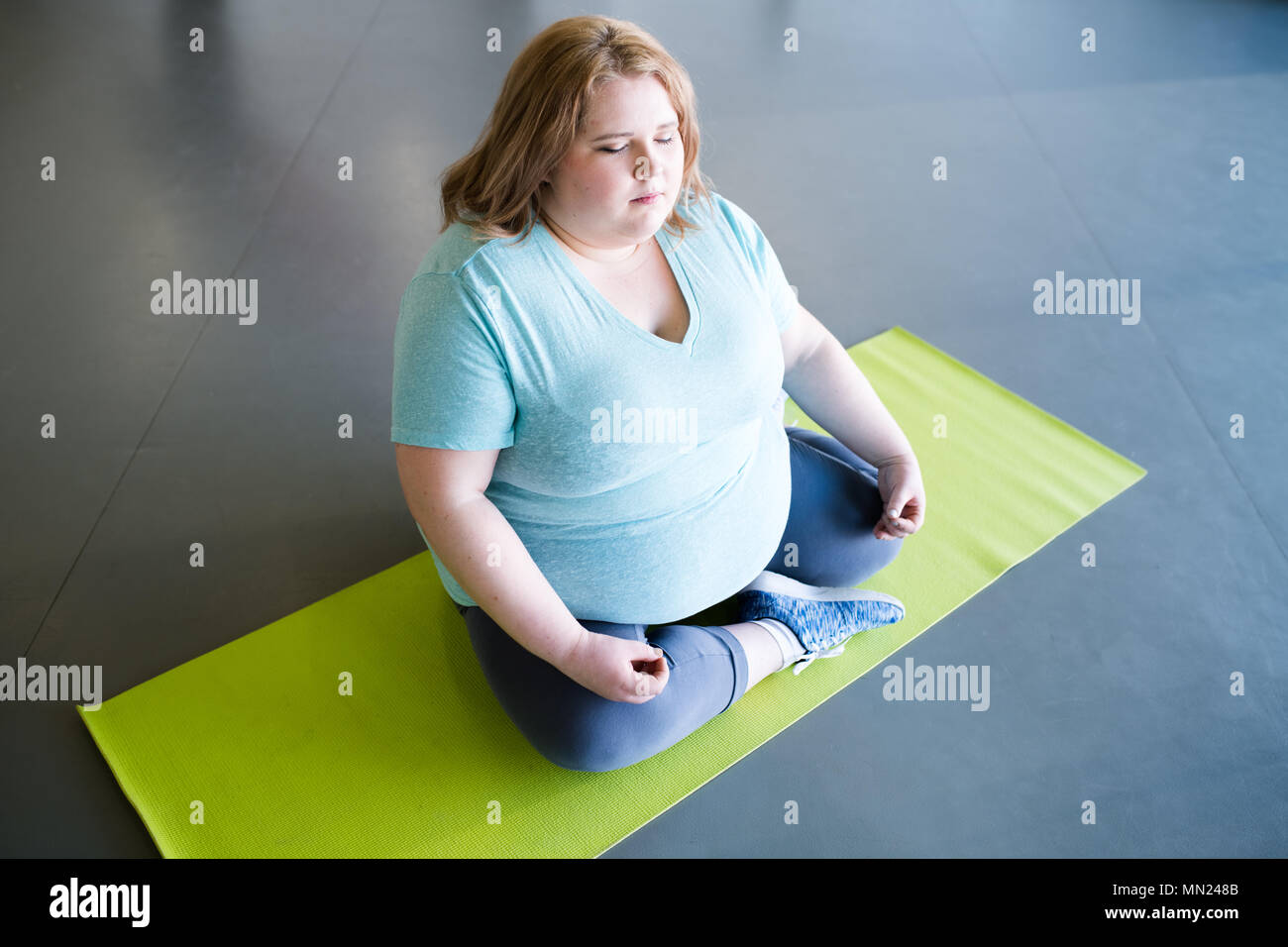 High angle portrait of obese young woman sitting in lotus position and ...