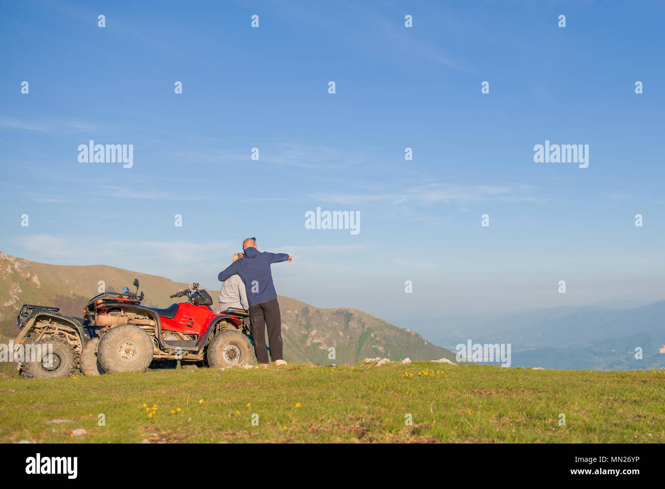 Rear view of young pair near atv. Man is showing something in distance ...