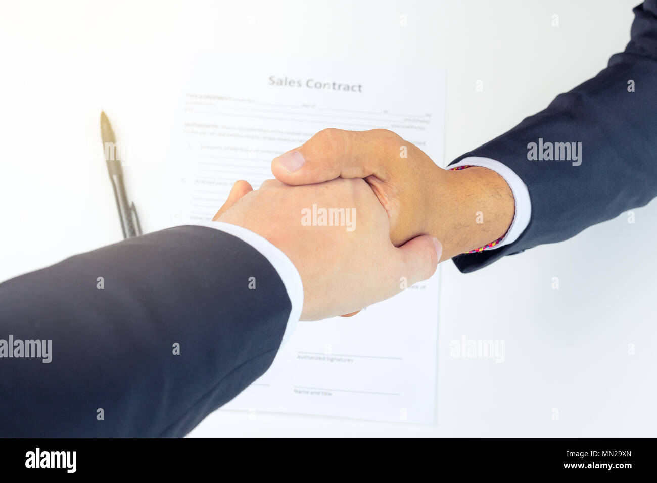Two business man shaking hands to each other above signed contract ...
