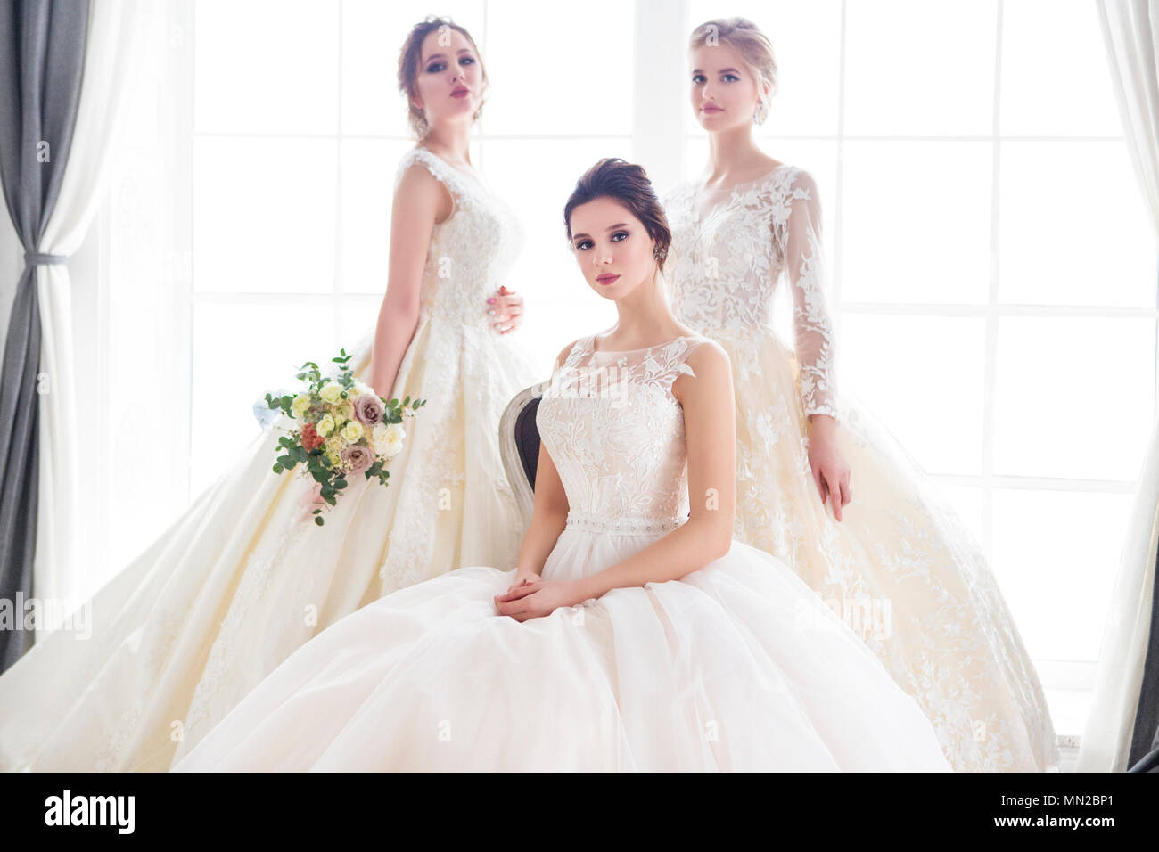 Three young woman with bouquets wearing wedding dresses Stock Photo - Alamy