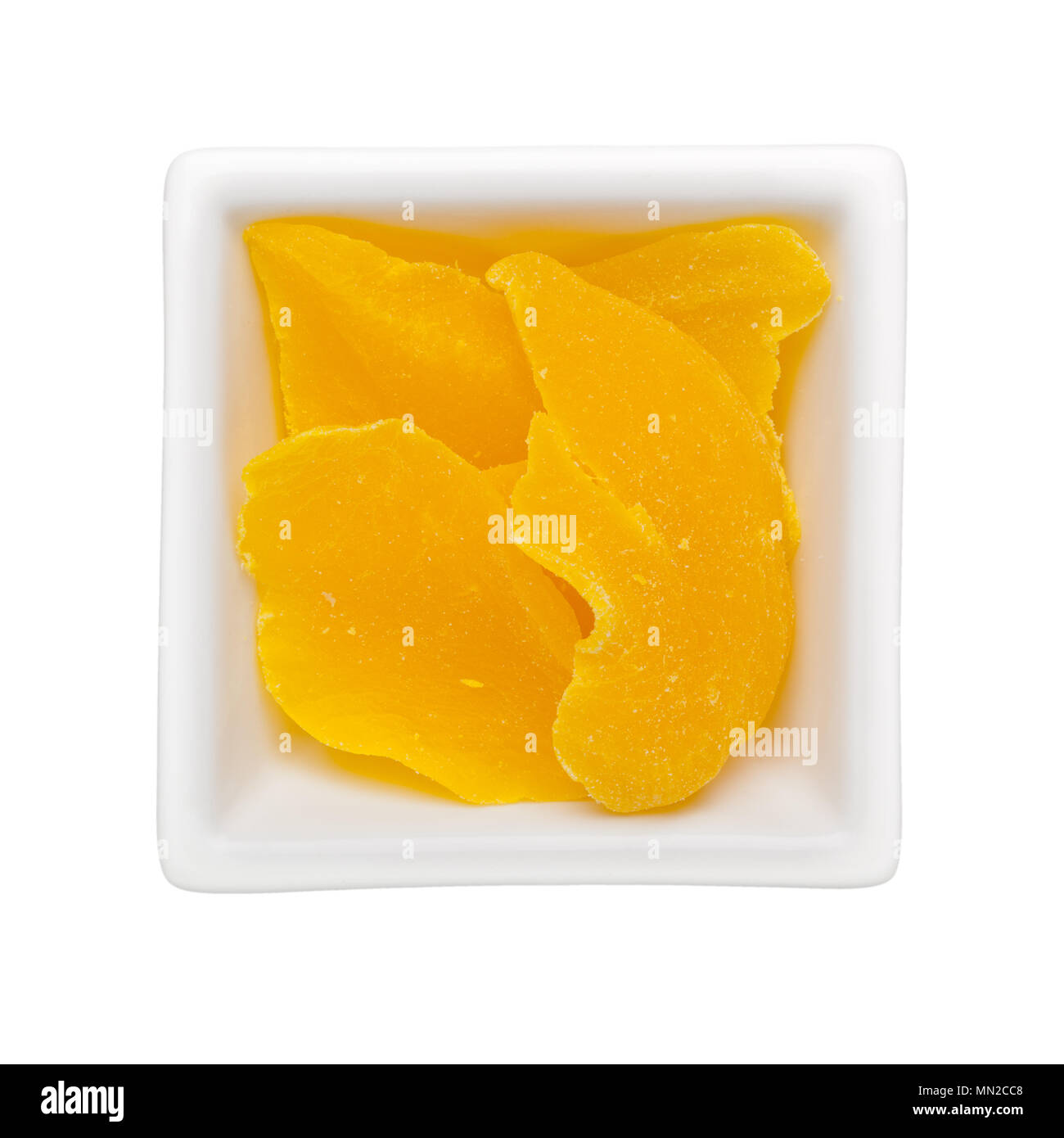 Pieces of candied mango in a square bowl isolated on white background ...