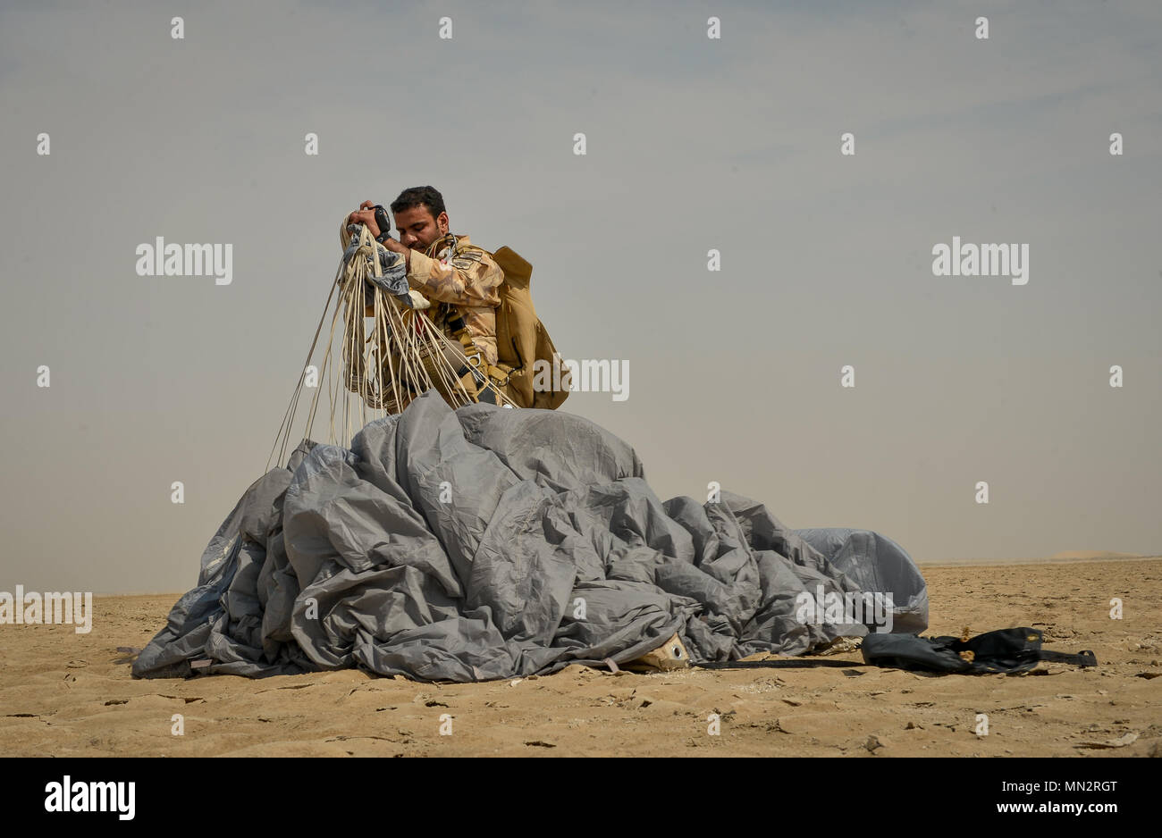 A Qatari service member packs up his parachute after conducting a ...