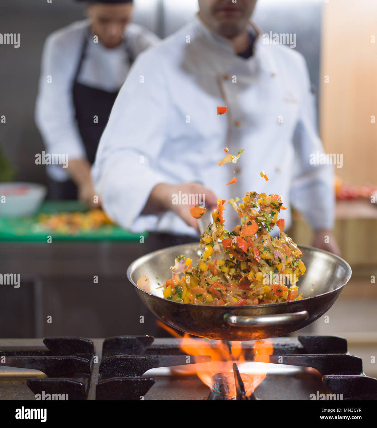 Young male chef flipping vegetables in wok at commercial kitchen Stock ...