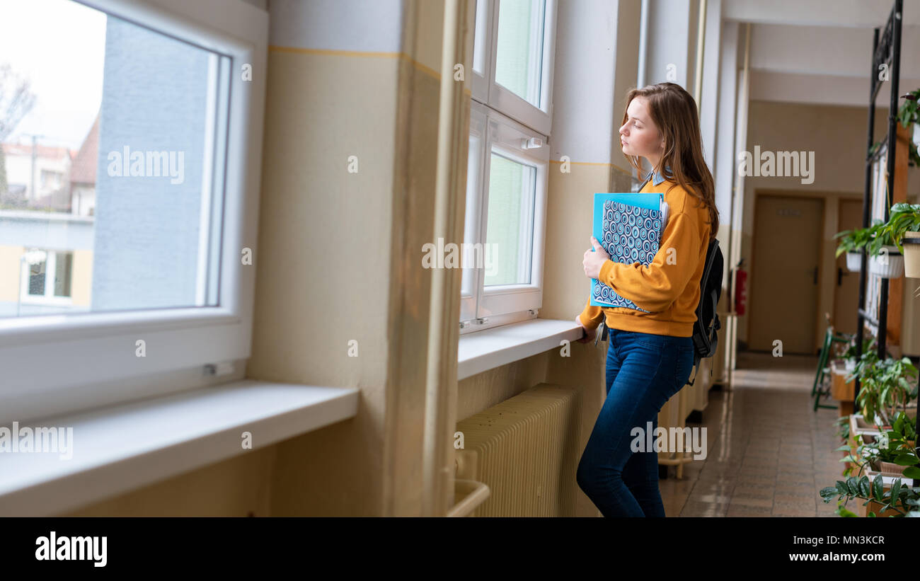 Young attractive female high school student standing by the window in ...
