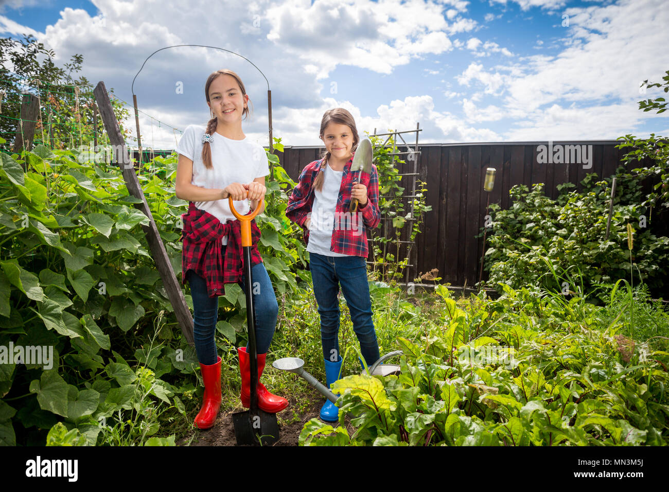 Two teenage girls posing in garden with gardening tools Stock Photo - Alamy
