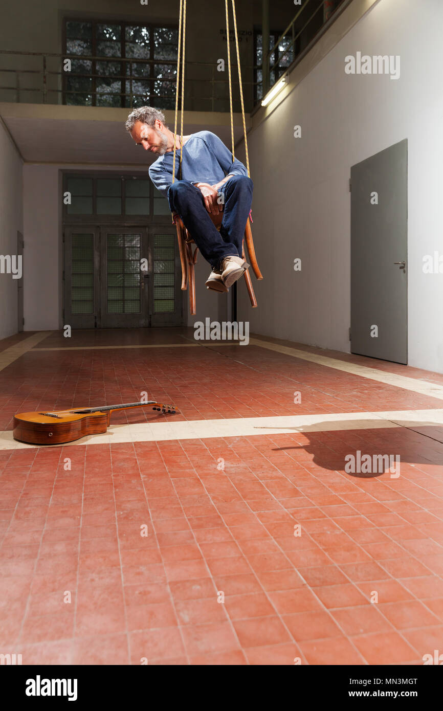 interior of an old factory, hanging man, sitting on the chair, portrait ...
