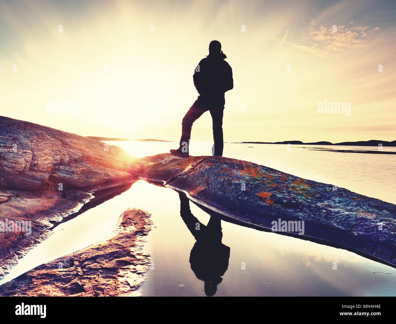 Silhouette of man in outdoor clothes on rocky cliff above sea ...