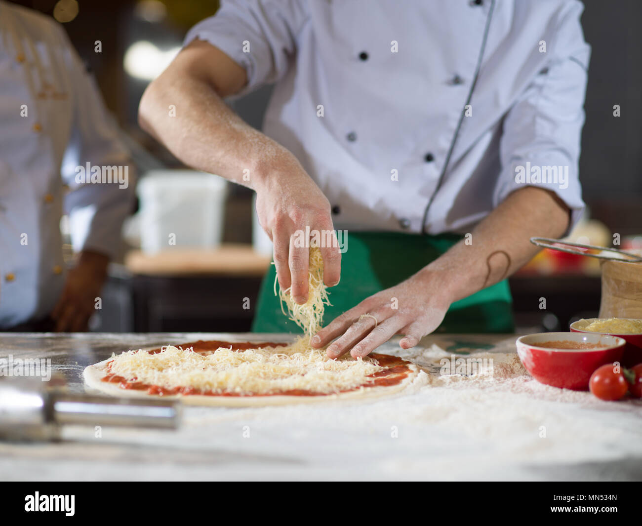 chef sprinkling cheese over fresh pizza dough on kitchen table Stock ...
