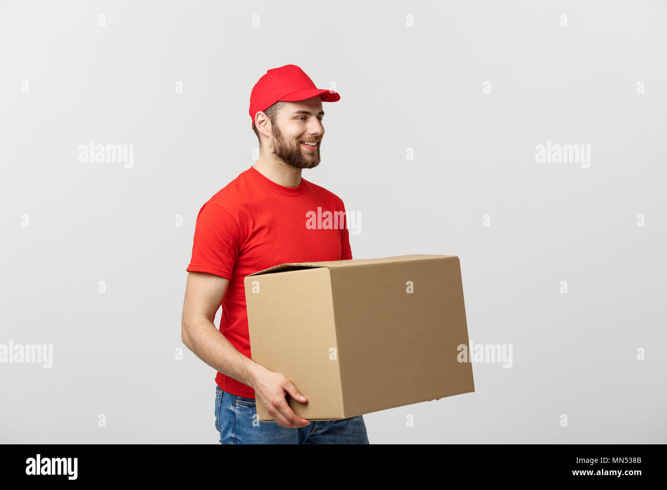 Young smiling logistic delivery man in red uniform holding the box on ...