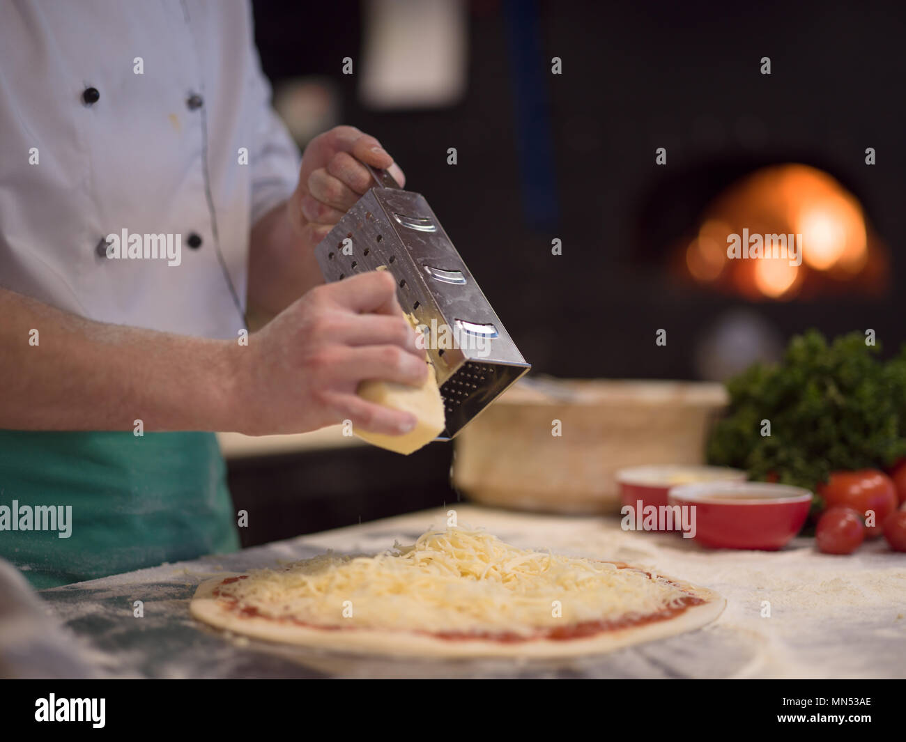 chef sprinkling cheese over fresh pizza dough on kitchen table Stock ...