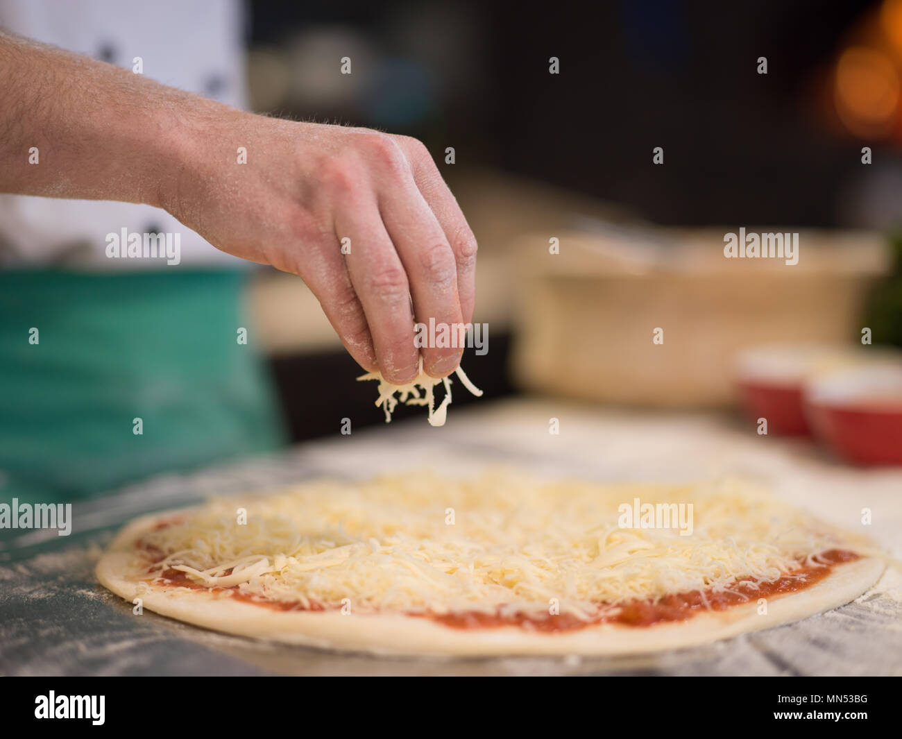 chef sprinkling cheese over fresh pizza dough on kitchen table Stock ...