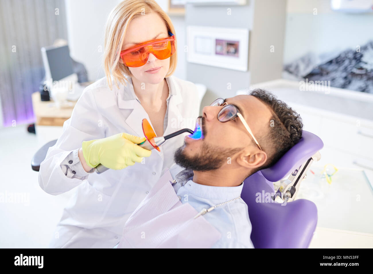 Portrait of female dentist whitening teeth of modern Middle-Eastern man ...