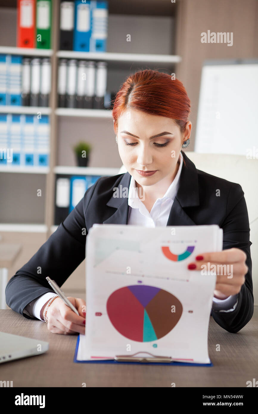 Businesswoman in formal suit in her office looking at documents and ...