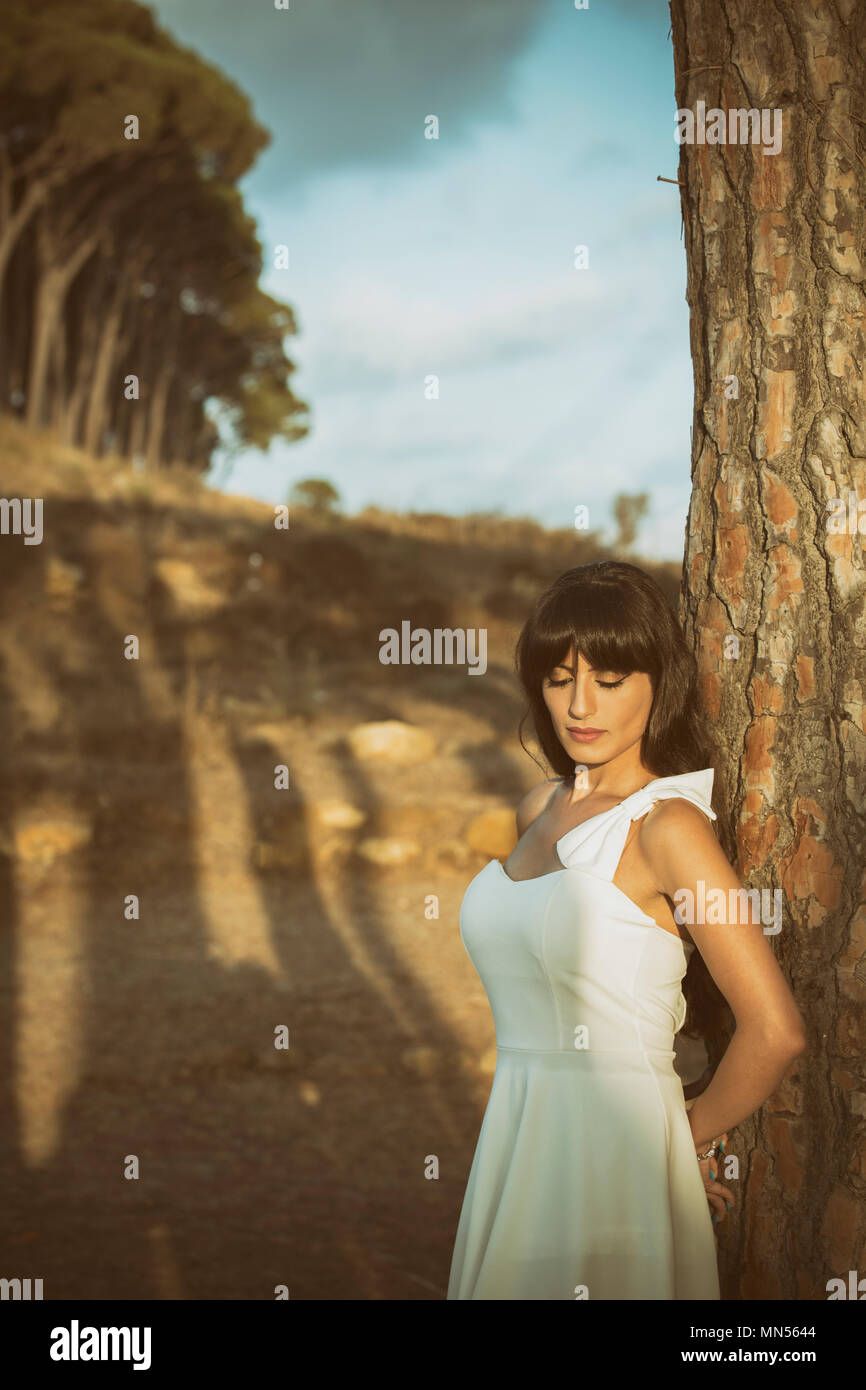 Beautiful woman leaning against a tree Stock Photo - Alamy