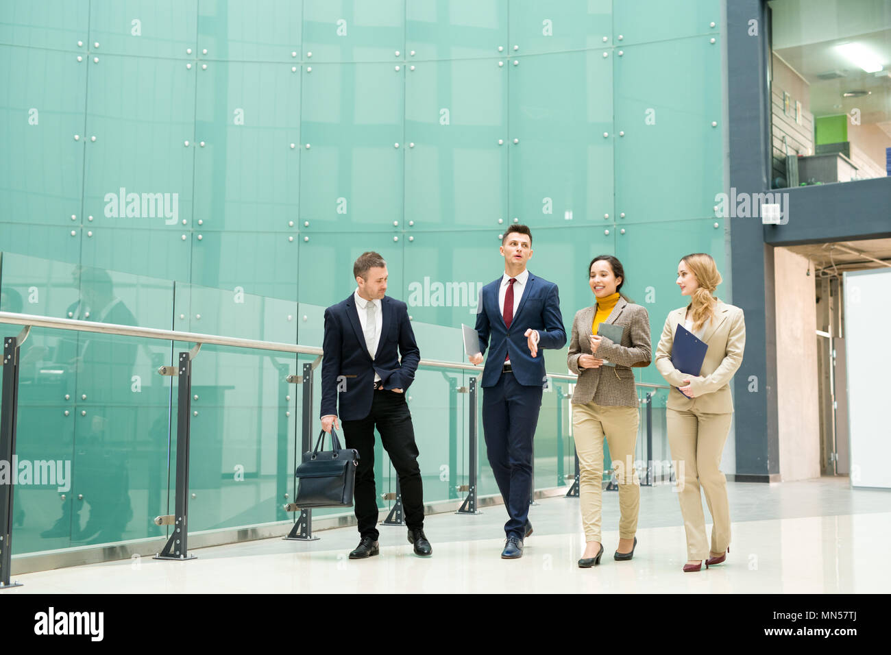 Full length portrait of four business people walking across hall of ...