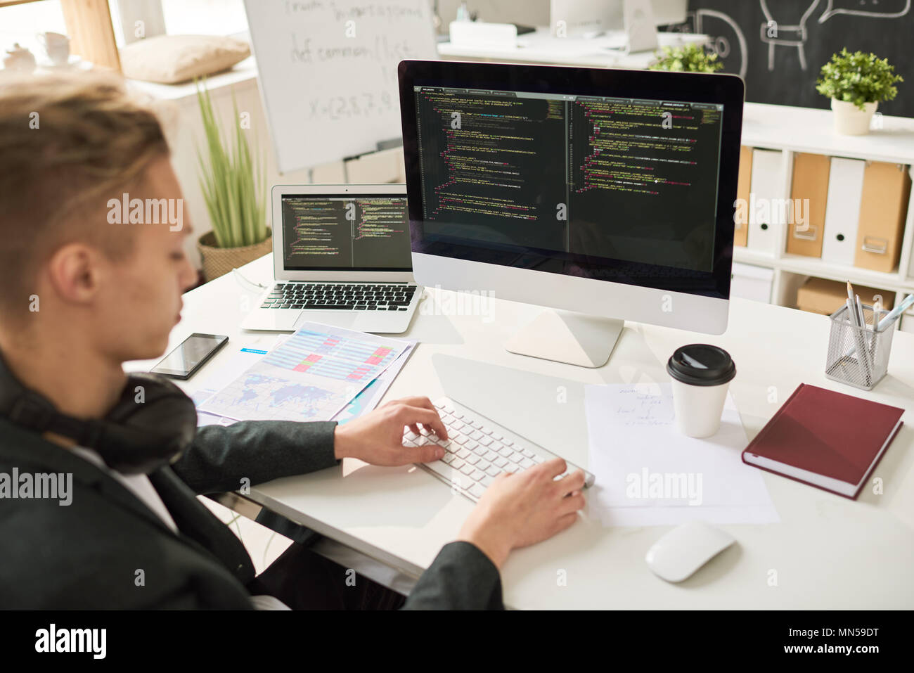 Portrait of contemporary young man coding at modern computer sitting at ...