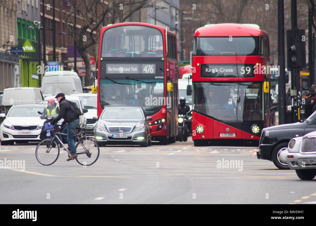 Two red London buses wait at crossroads as a bicycle crosses Stock Photo - Alamy