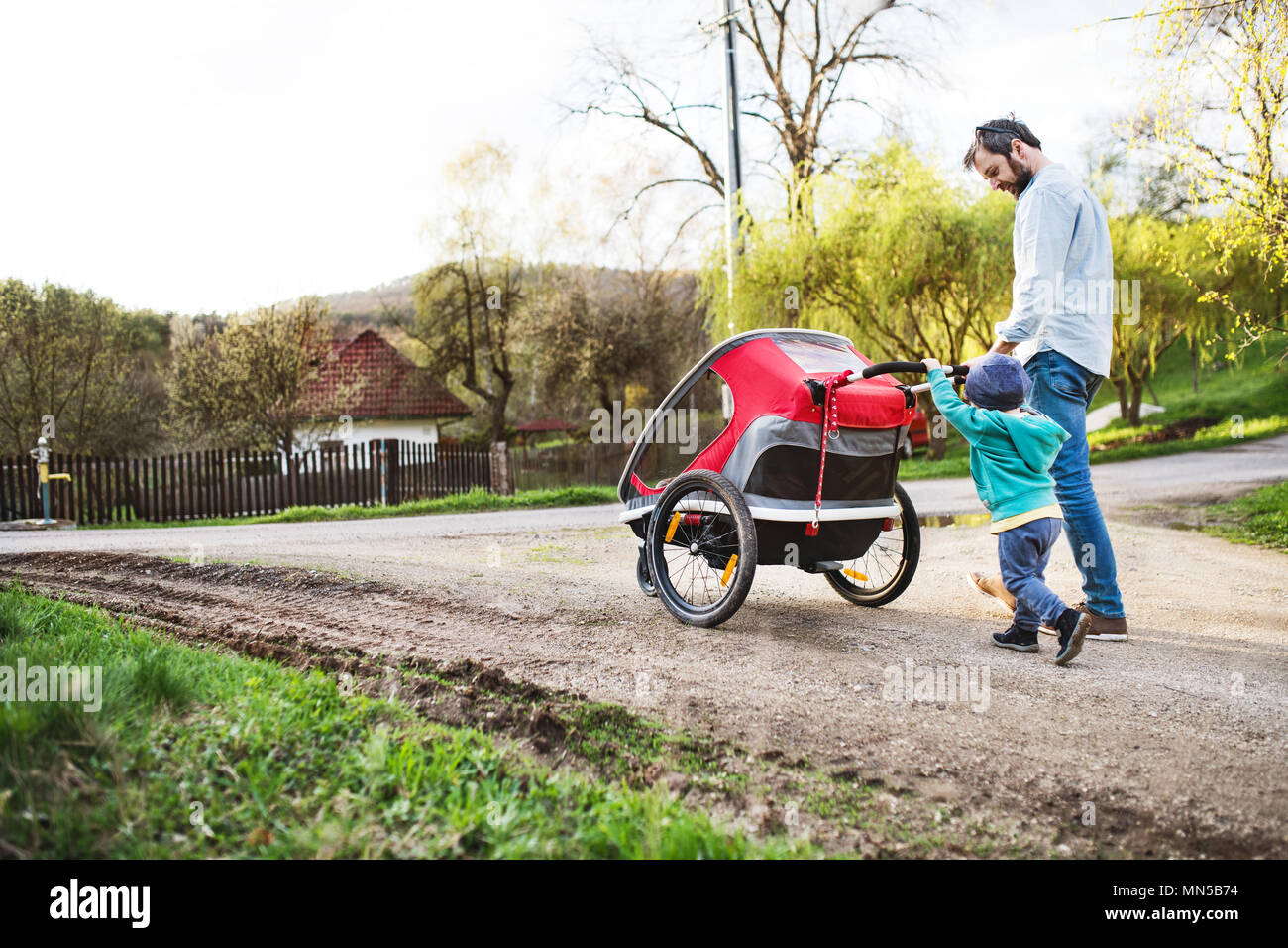 A father with toddler son pushing a jogging stroller outside. A walk in ...
