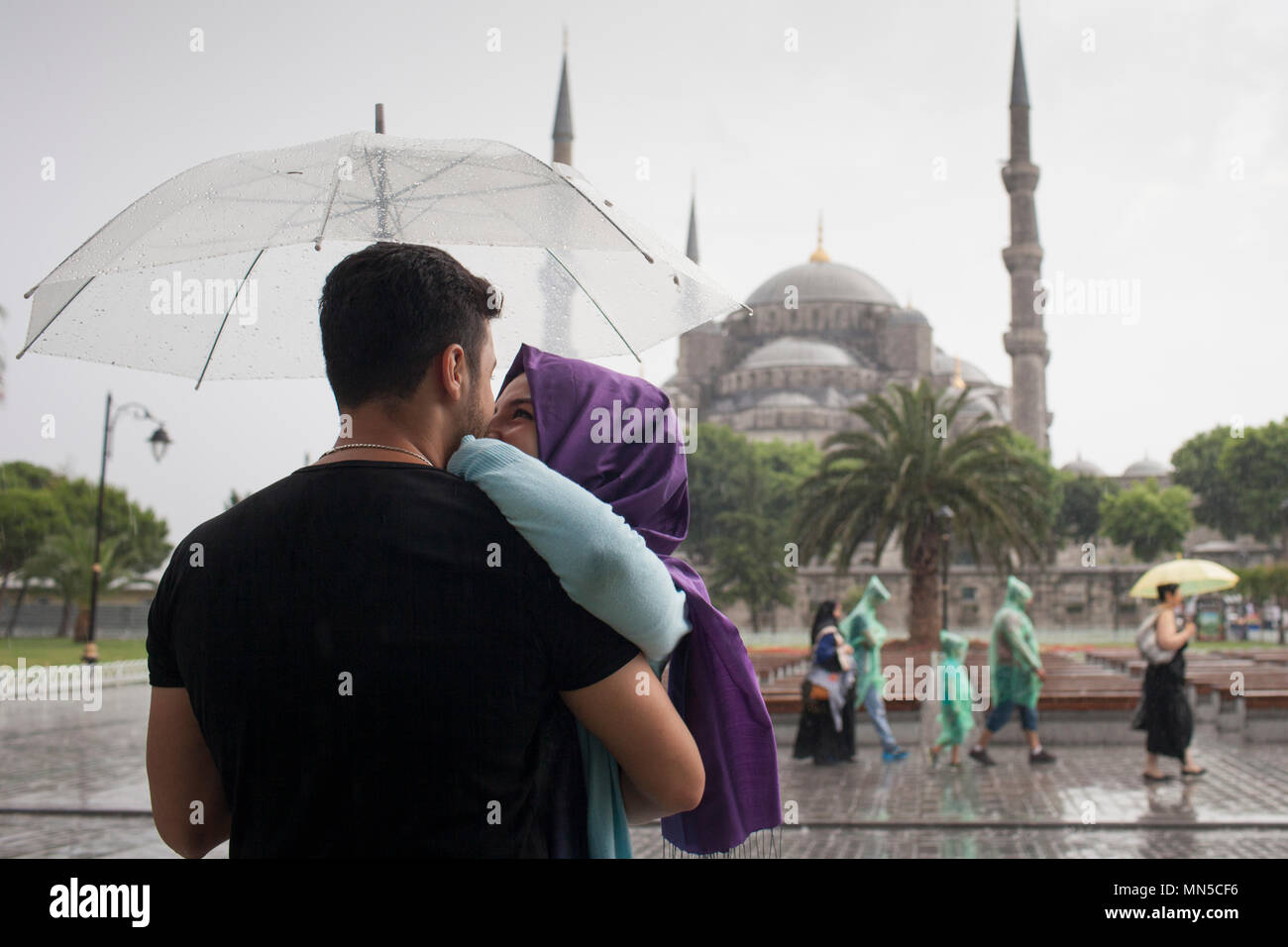 Couple sheltering under umbrella in rain storm by the blue mosque ...