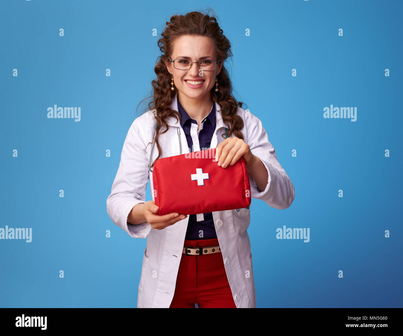 smiling physician woman in white medical robe showing first-aid kit ...