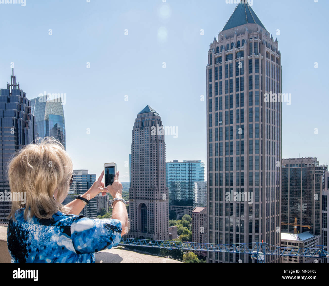Woman taking a picture with her cell phone of a midtown skyline. She is ...