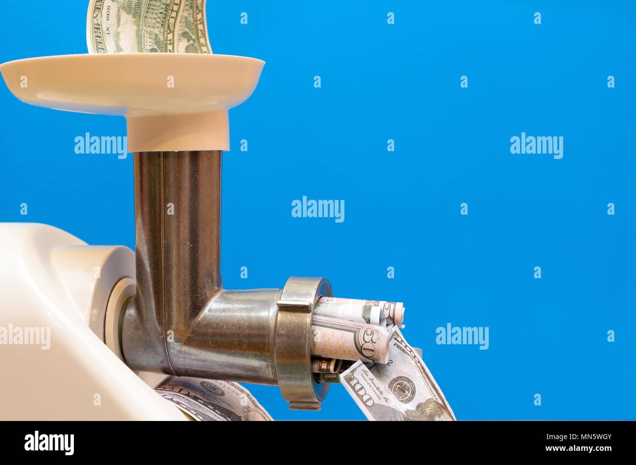Money passes through a meat grinder. Blue background Stock Photo - Alamy
