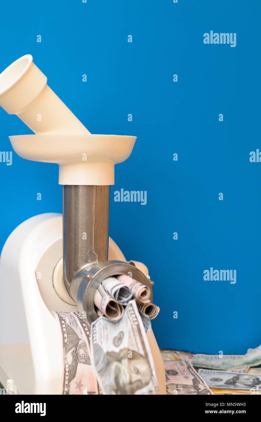 Money passes through a meat grinder. Blue background Stock Photo - Alamy