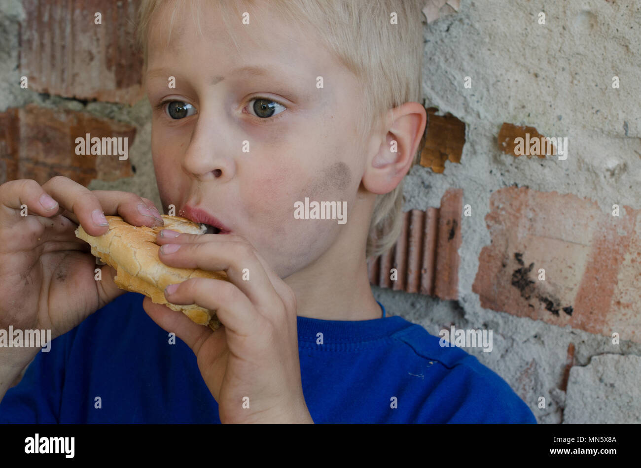 A hungry dirty boy greedily eats a crust of bread against the wall ...