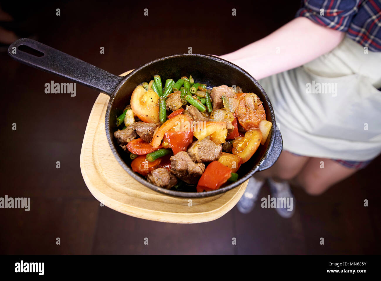 Cooked hot meat with vegetables in a frying pan in the hands of the ...