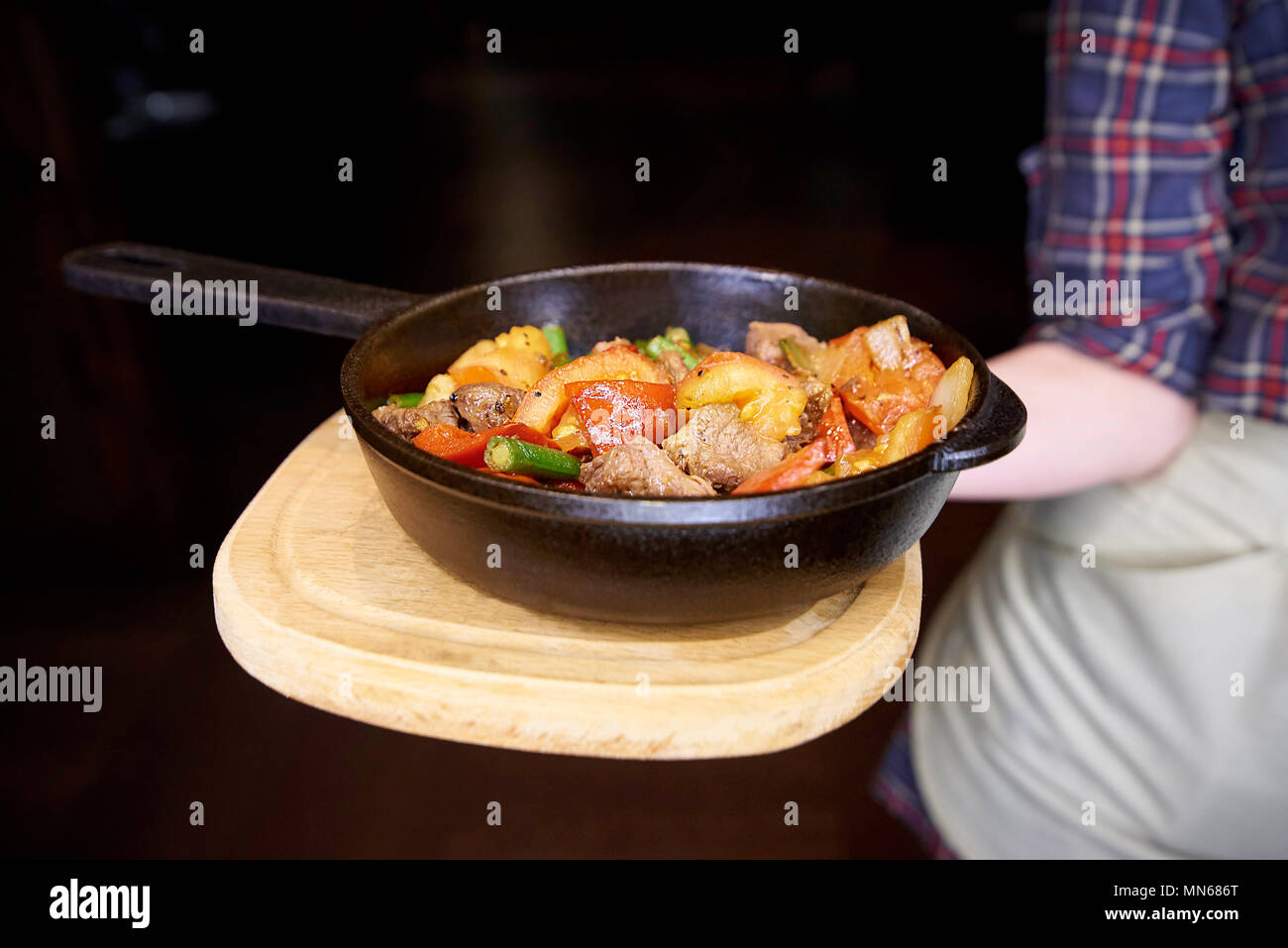 Cooked hot meat with vegetables in a frying pan in the hands of the ...