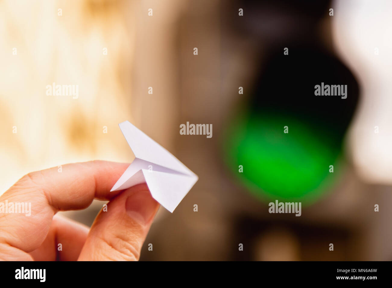 One small paper airplane in hand against a traffic light background ...