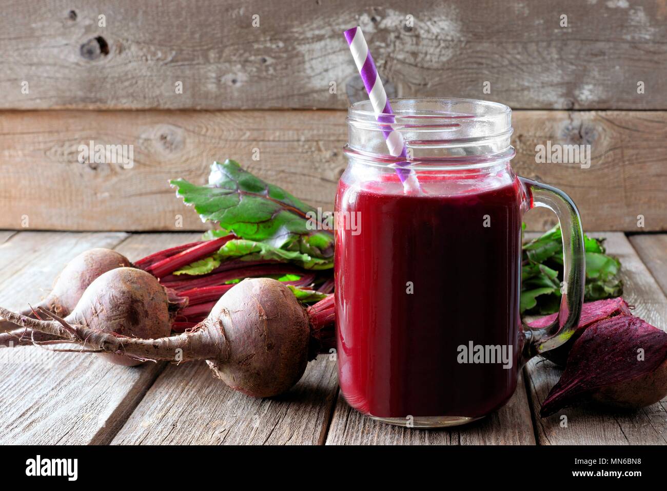 Fresh beet juice in a mason jar glass with beets over a rustic wood ...