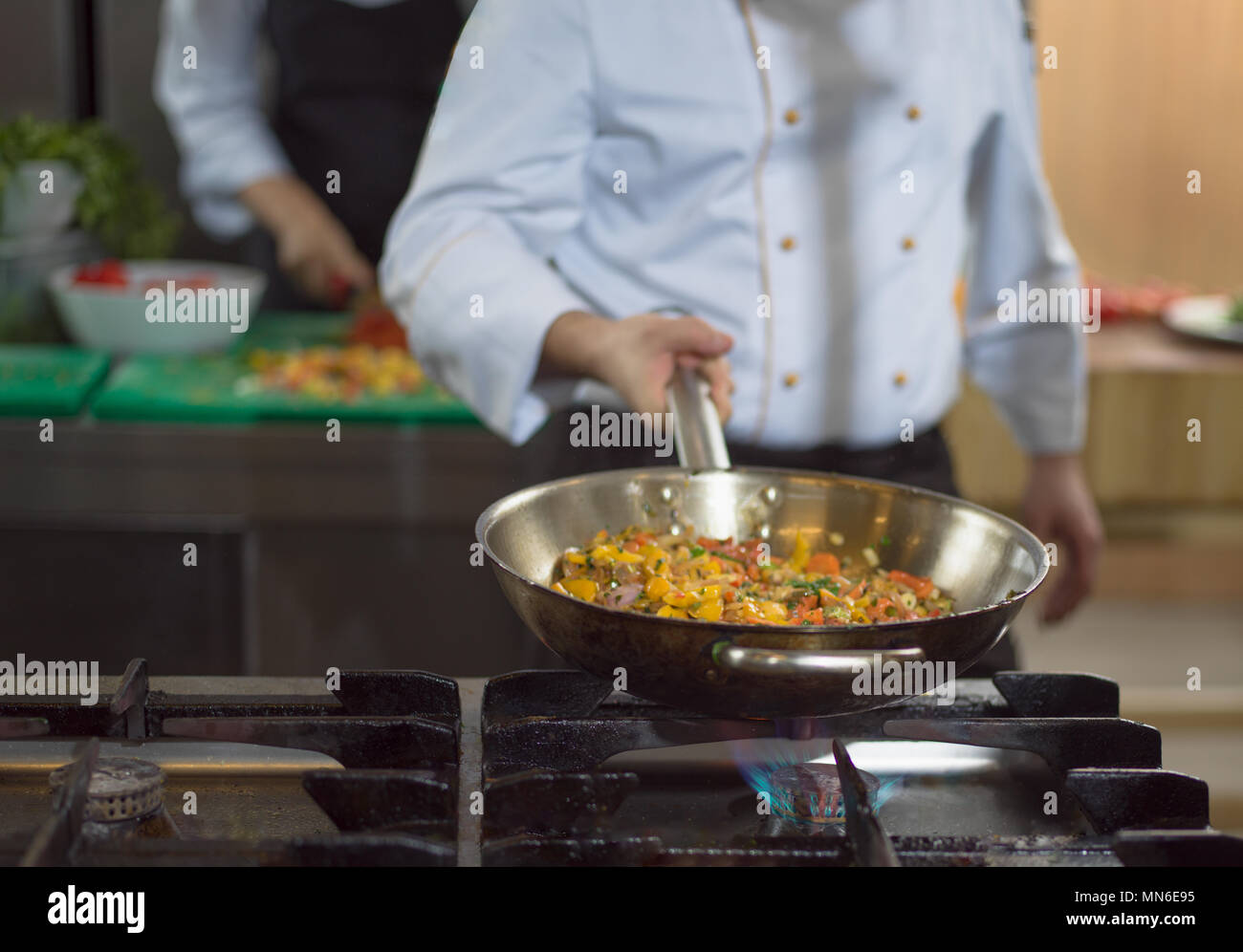 Young male chef flipping vegetables in wok at commercial kitchen Stock ...