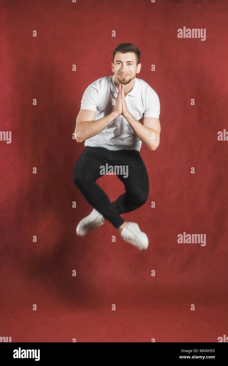 Photo of a young man on a red wall background looking at camera jumping ...