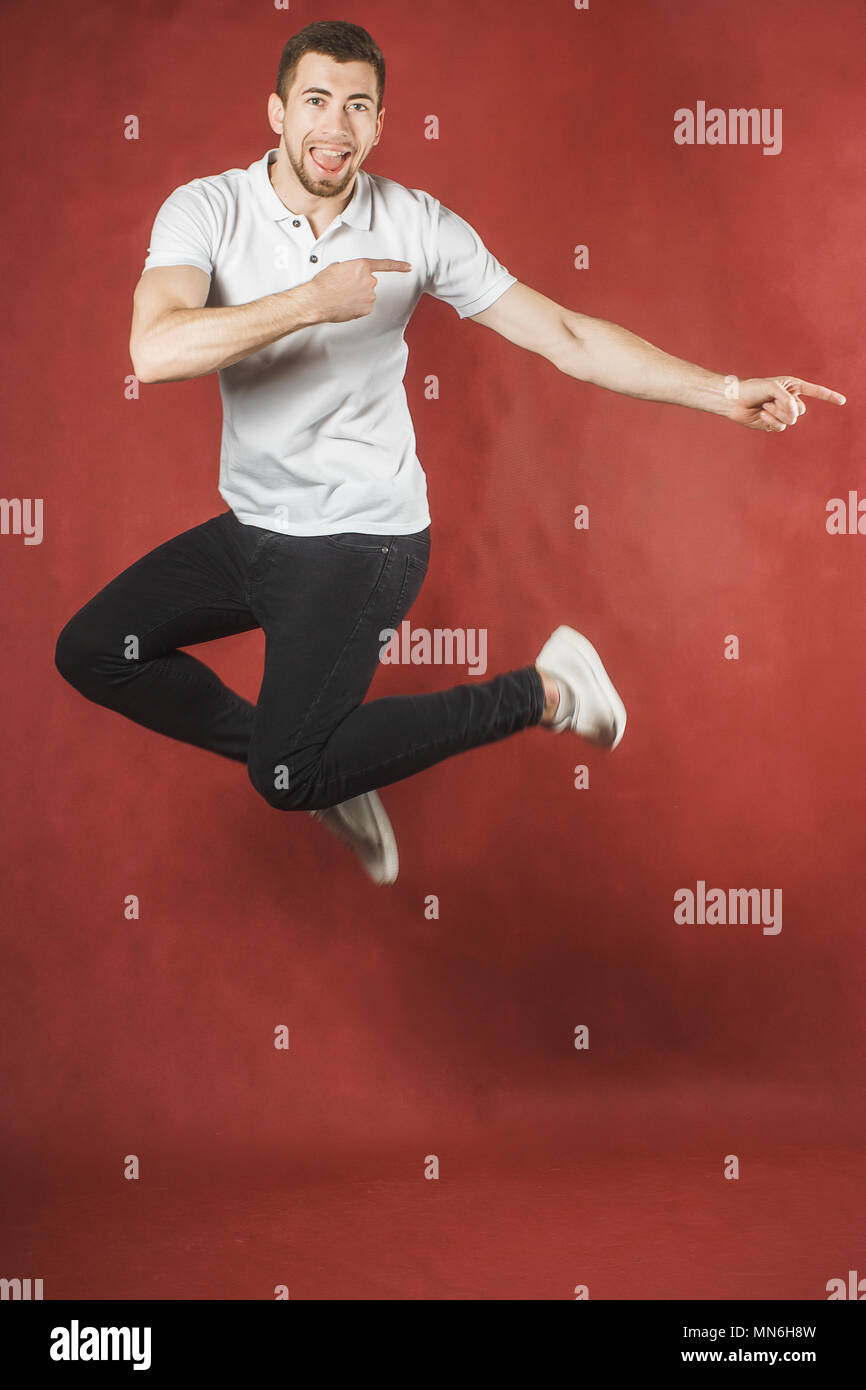Photo of a young man on a red wall background looking at camera jumping ...