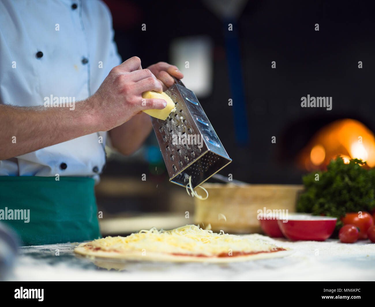 chef sprinkling cheese over fresh pizza dough on kitchen table Stock ...