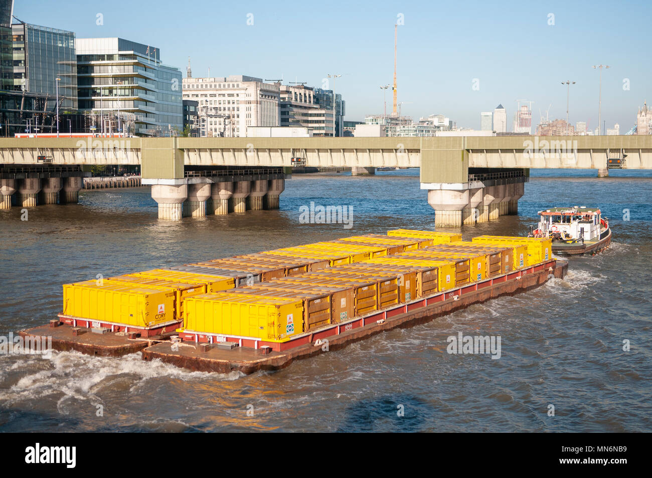 Tug tows barges holding yellow shipping containers filled with general ...