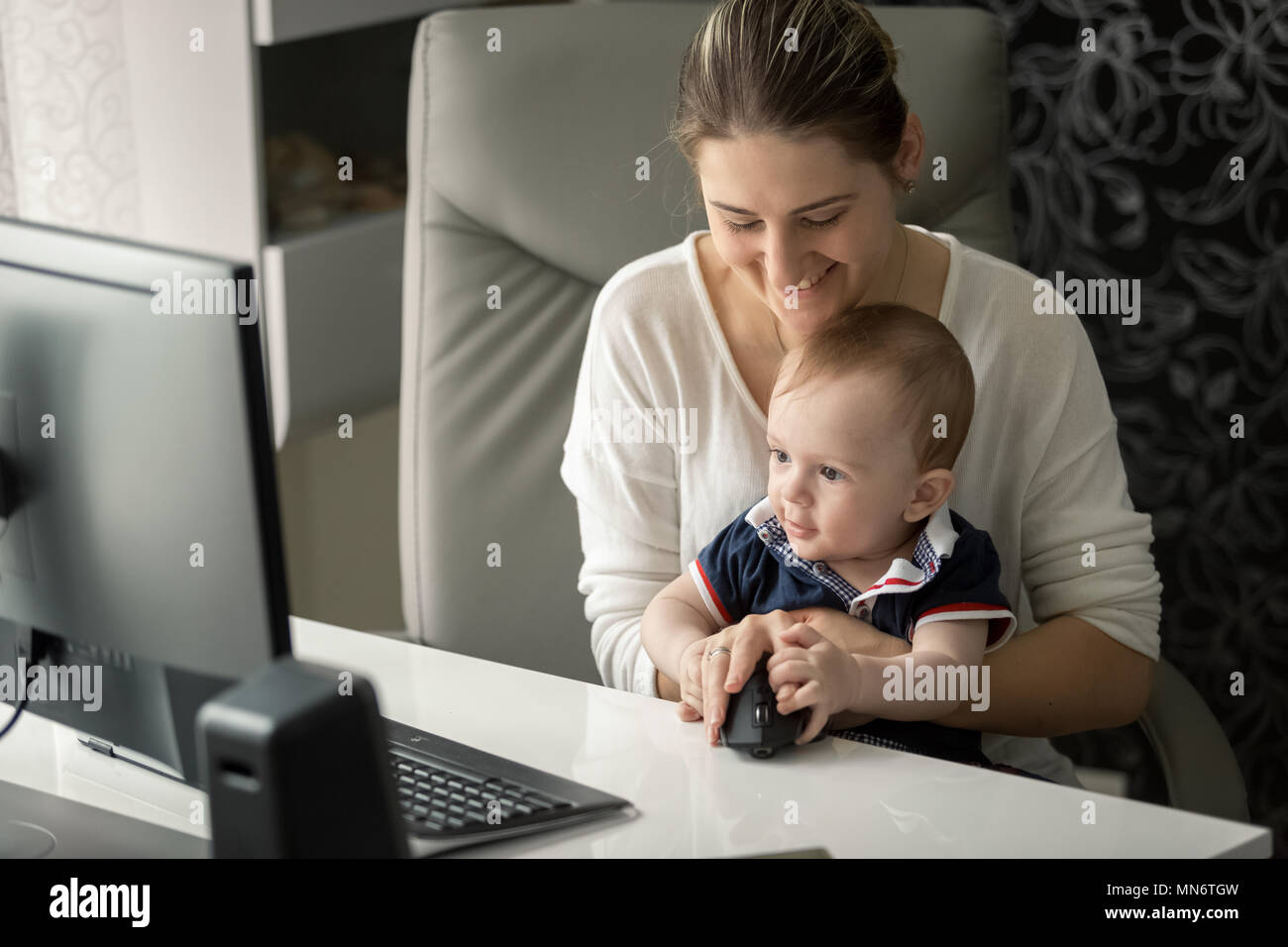 Portrait of smiling young mother showing her baby son how to use ...