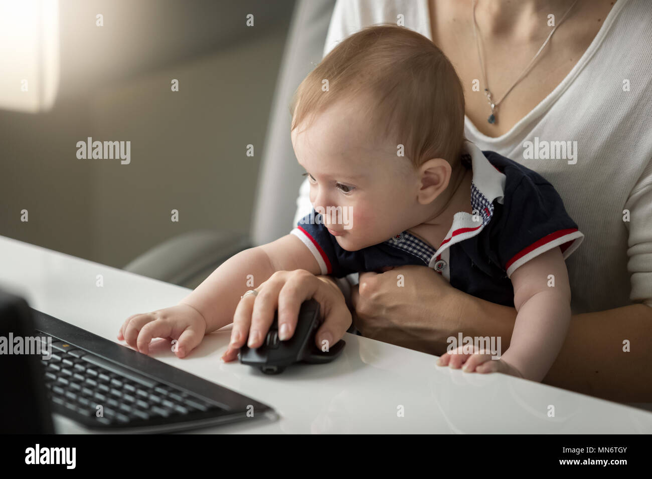Portrait of cute little baby boy sitting on mothers lap and reaching ...