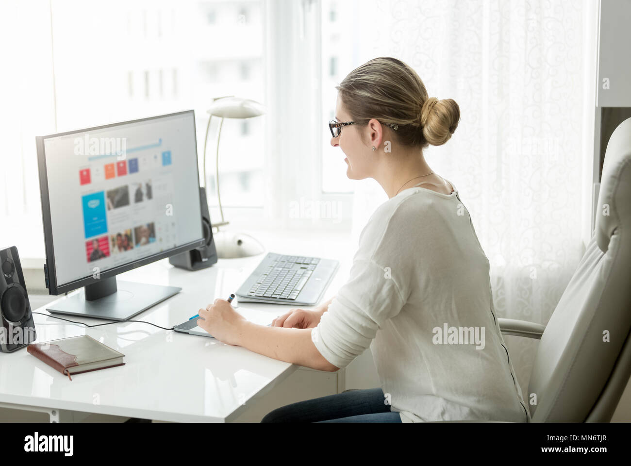 Beautiful young woman working on computer at office with big window ...