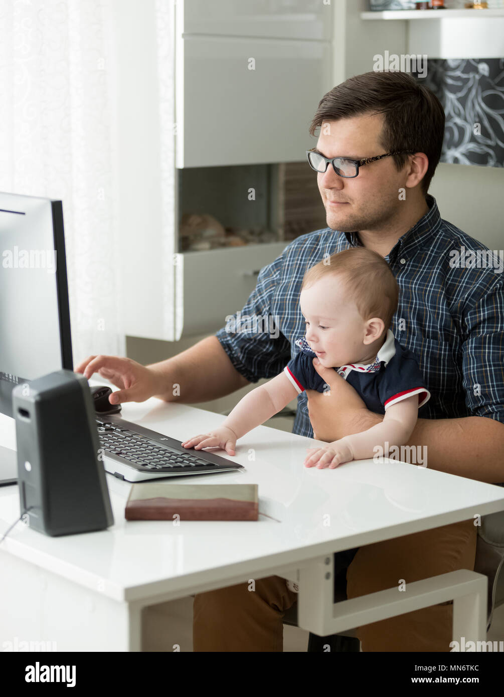 Portrait of young man working at office and holding his 1 year old baby ...