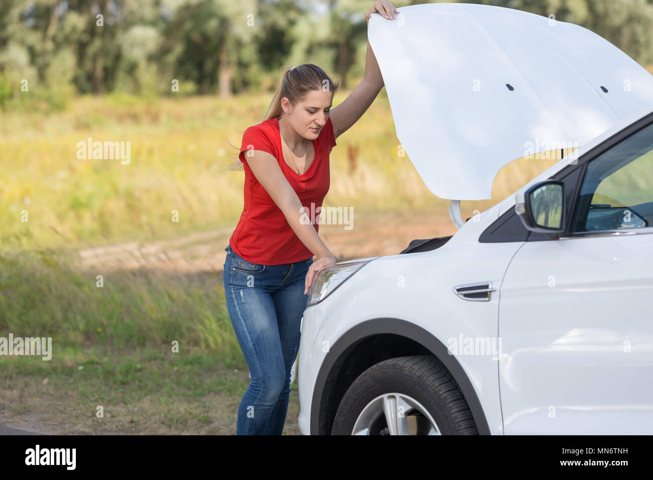 Portrait of young upset woman looking under the hood of broken car Stock Photo - Alamy