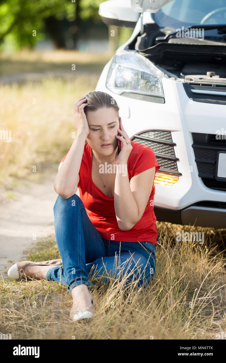 Young crying woman sitting at her broken car in field and calling auto ...