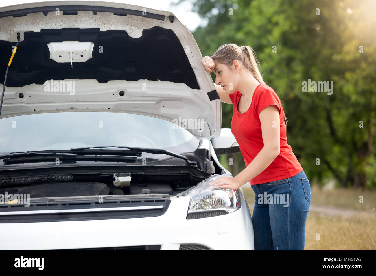 Portrait of sad young woman leaning on open car hood and looking at broken engine Stock Photo ...