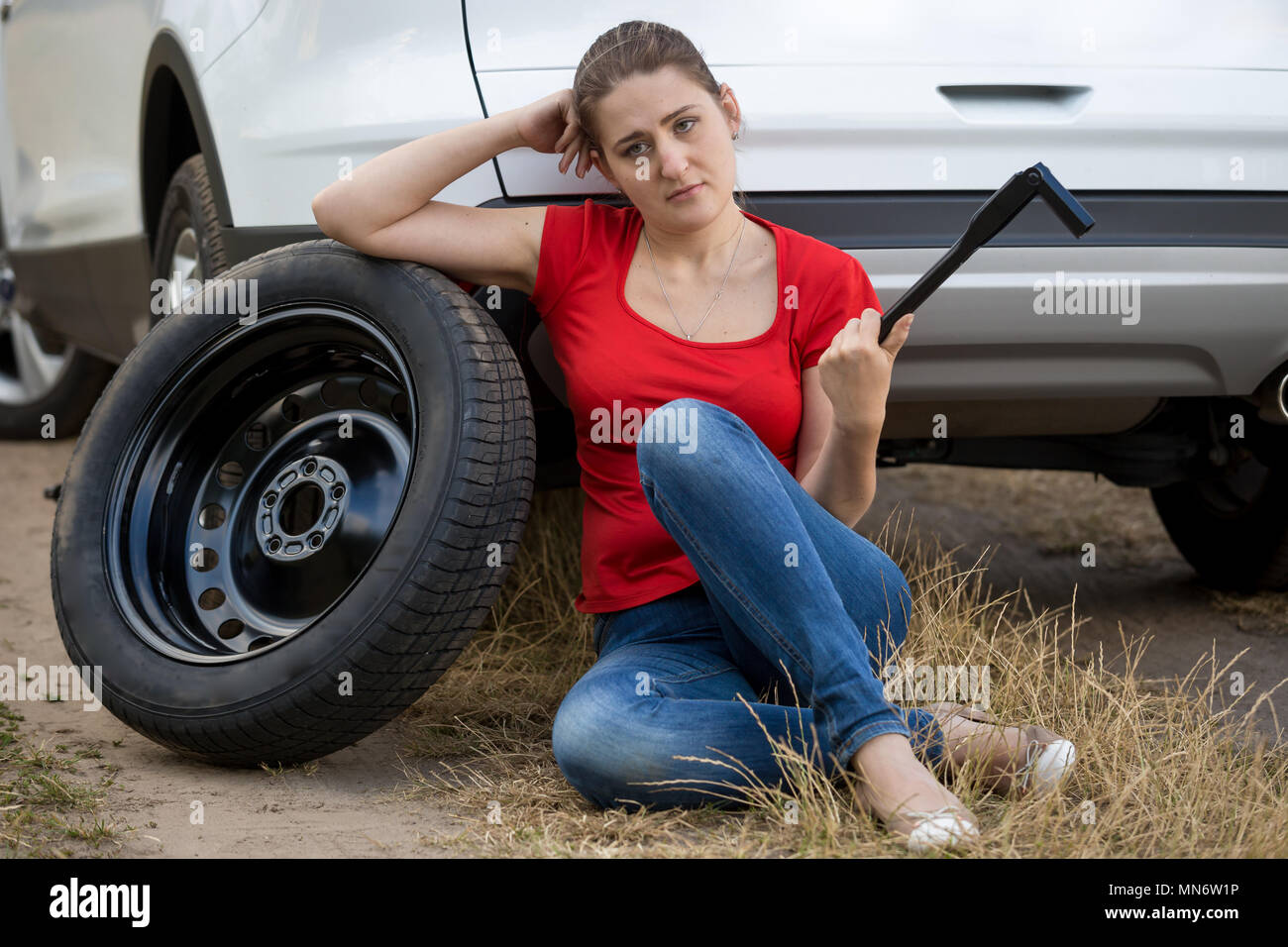 Portrait of young woman sitting at broken caar in field and holding car ...