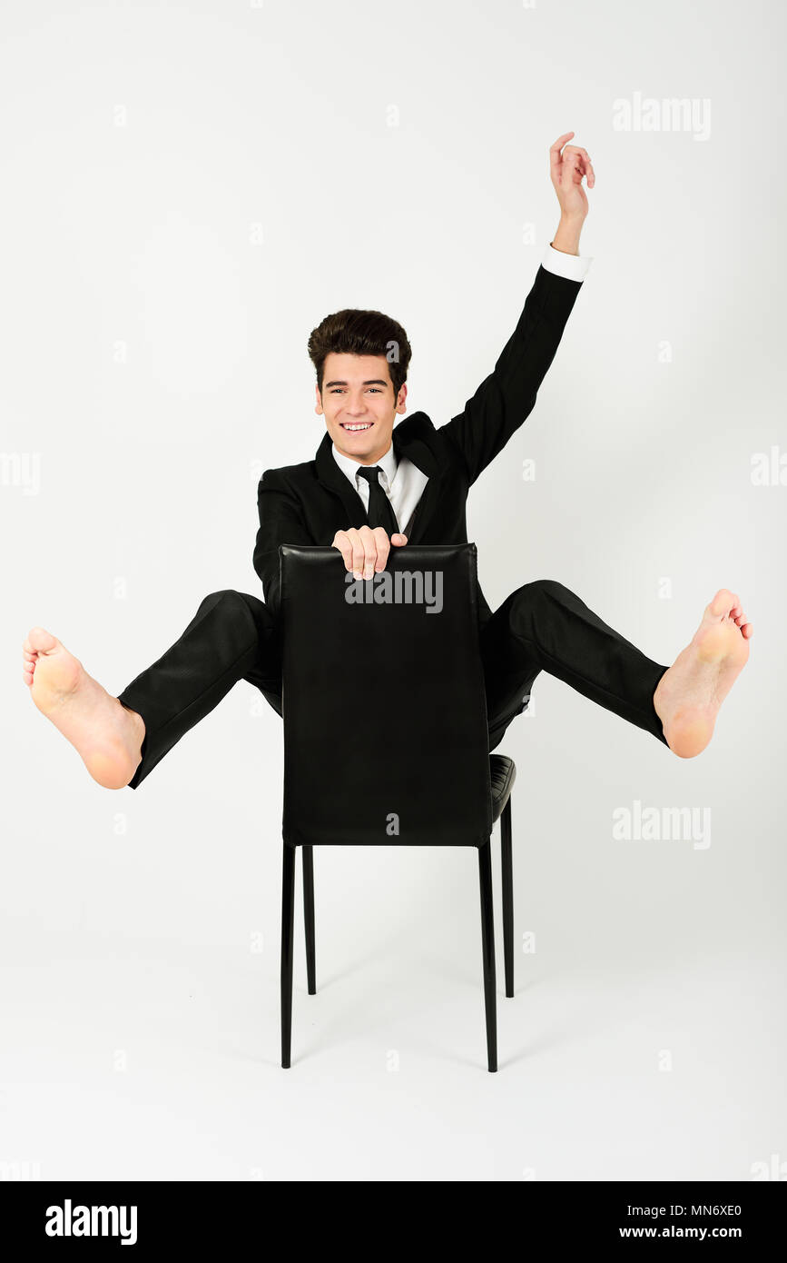 Portrait of a happy young businessman sitting in a chair with raised ...