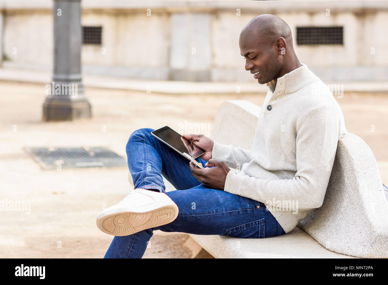 Black young man looking at tablet computer and smartphone in urban ...